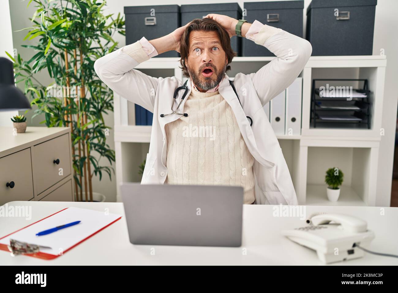 Handsome middle age doctor man working at the clinic crazy and scared ...