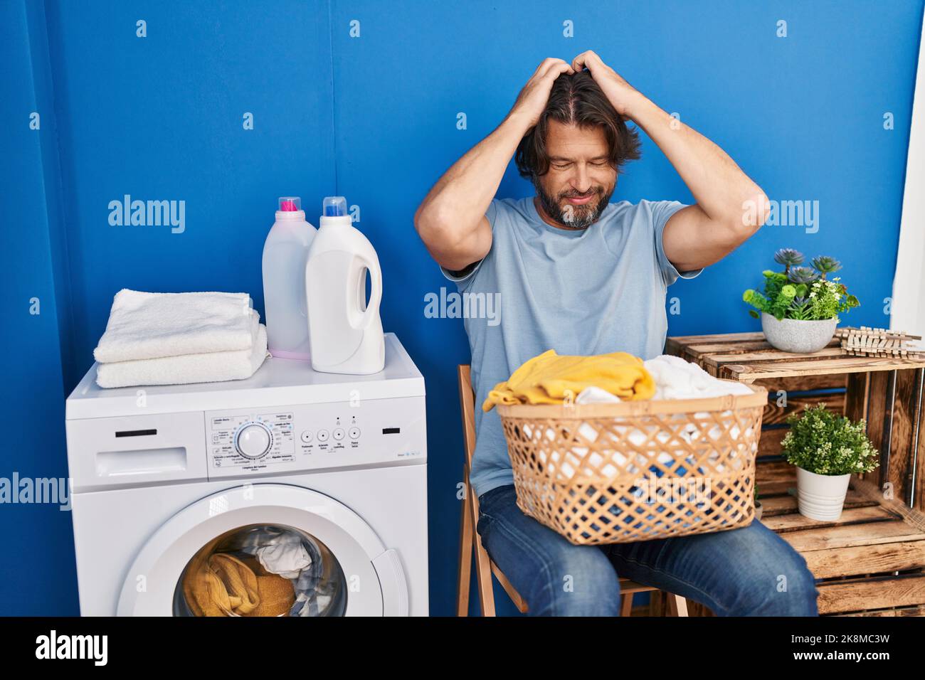 Handsome middle age man waiting for laundry suffering from headache ...