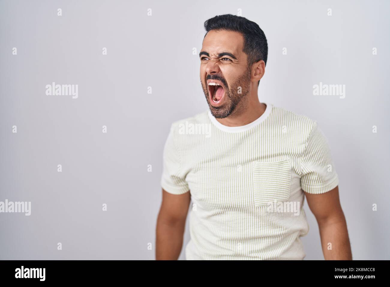 Hispanic man with beard standing over isolated background angry and mad ...