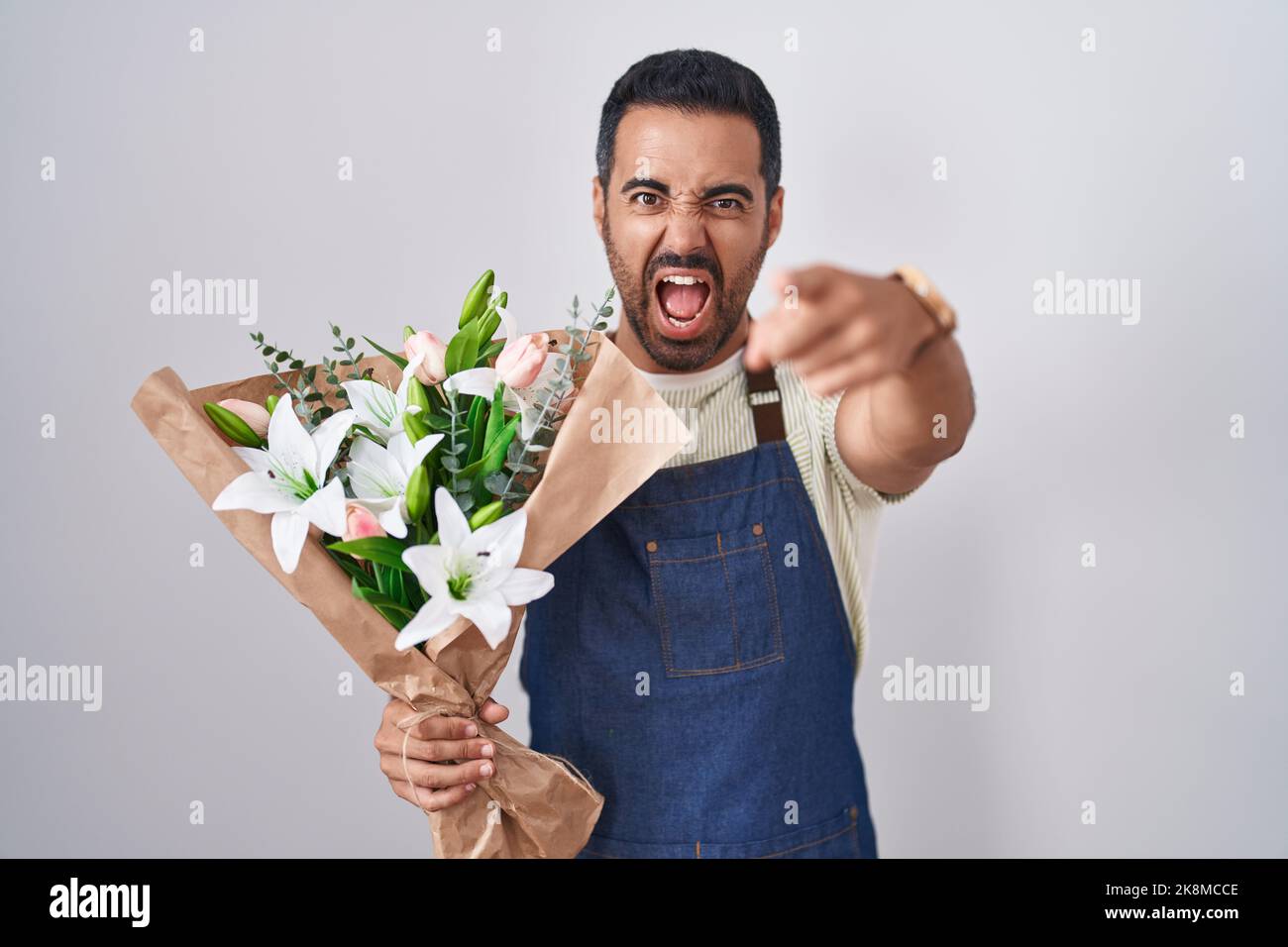 Hispanic man with beard working as florist pointing displeased and ...