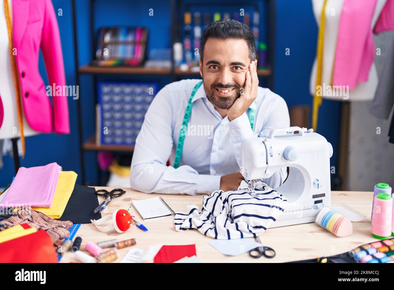 Young hispanic man tailor smiling confident sitting on table at sewing ...