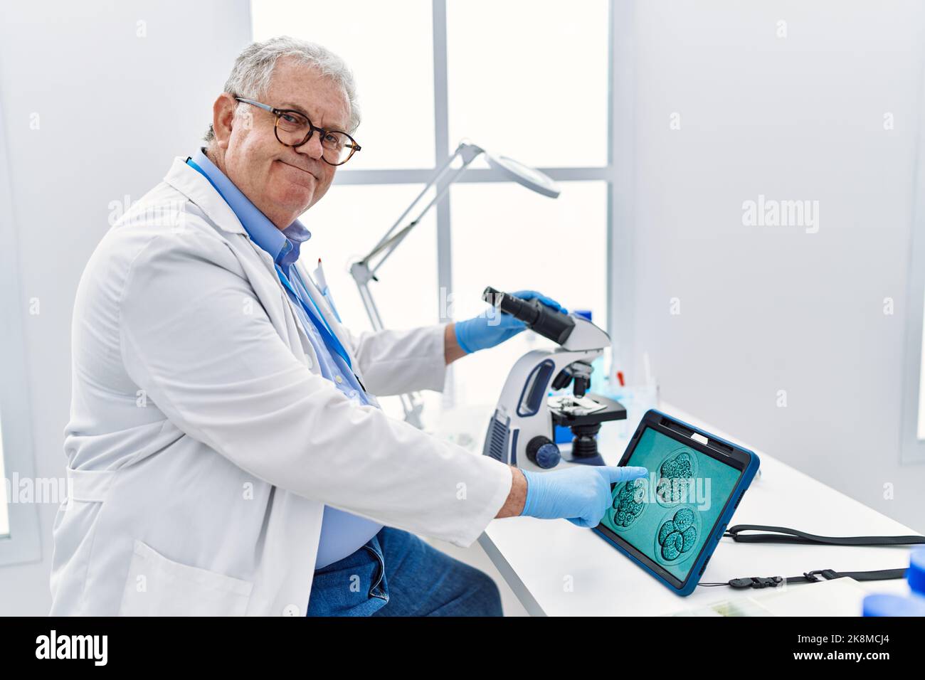 Middle age grey-haired man wearing scientist uniform looking embryology ...