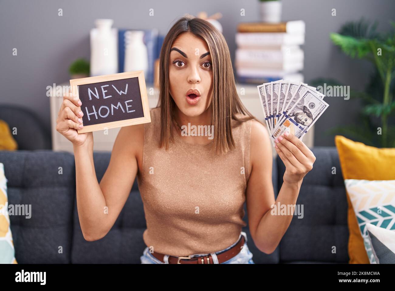 Young hispanic woman holding blackboard with new home text and dollars ...