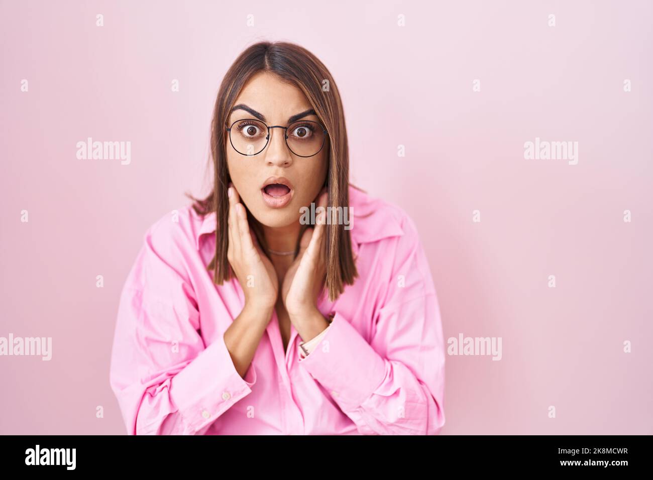 Young hispanic woman wearing glasses standing over pink background ...