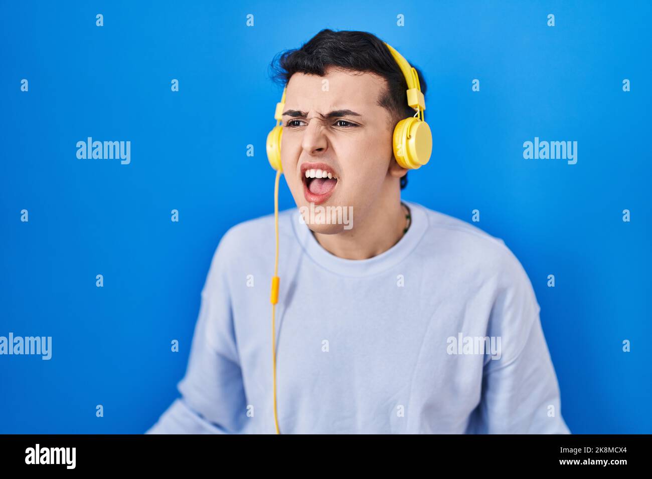 Non binary person listening to music using headphones angry and mad ...