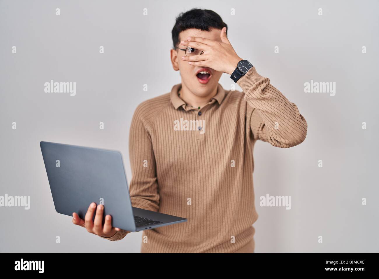 Non binary person using computer laptop peeking in shock covering face ...