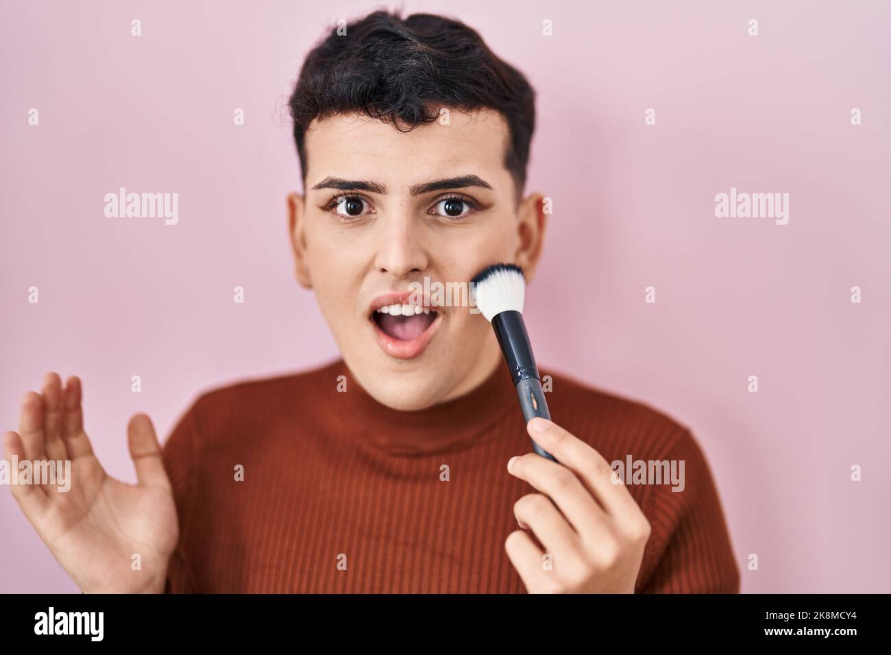 Non binary person applying make up scared and amazed with open mouth ...