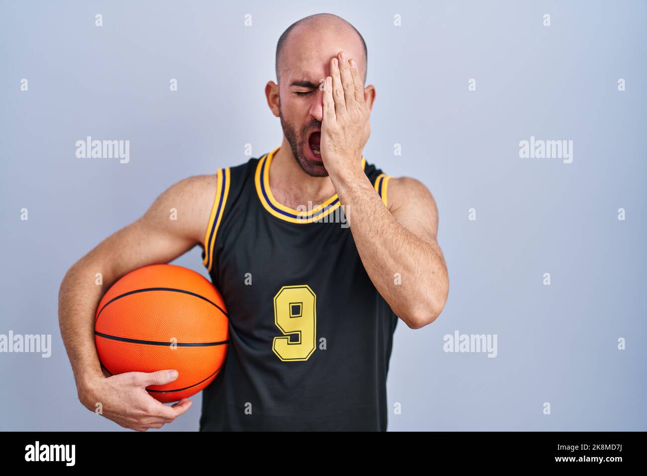 Young bald man with beard wearing basketball uniform holding ball ...