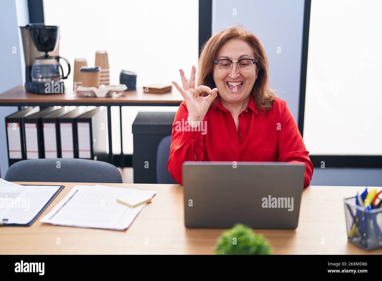 Senior woman with glasses working at the office with laptop doing ok ...