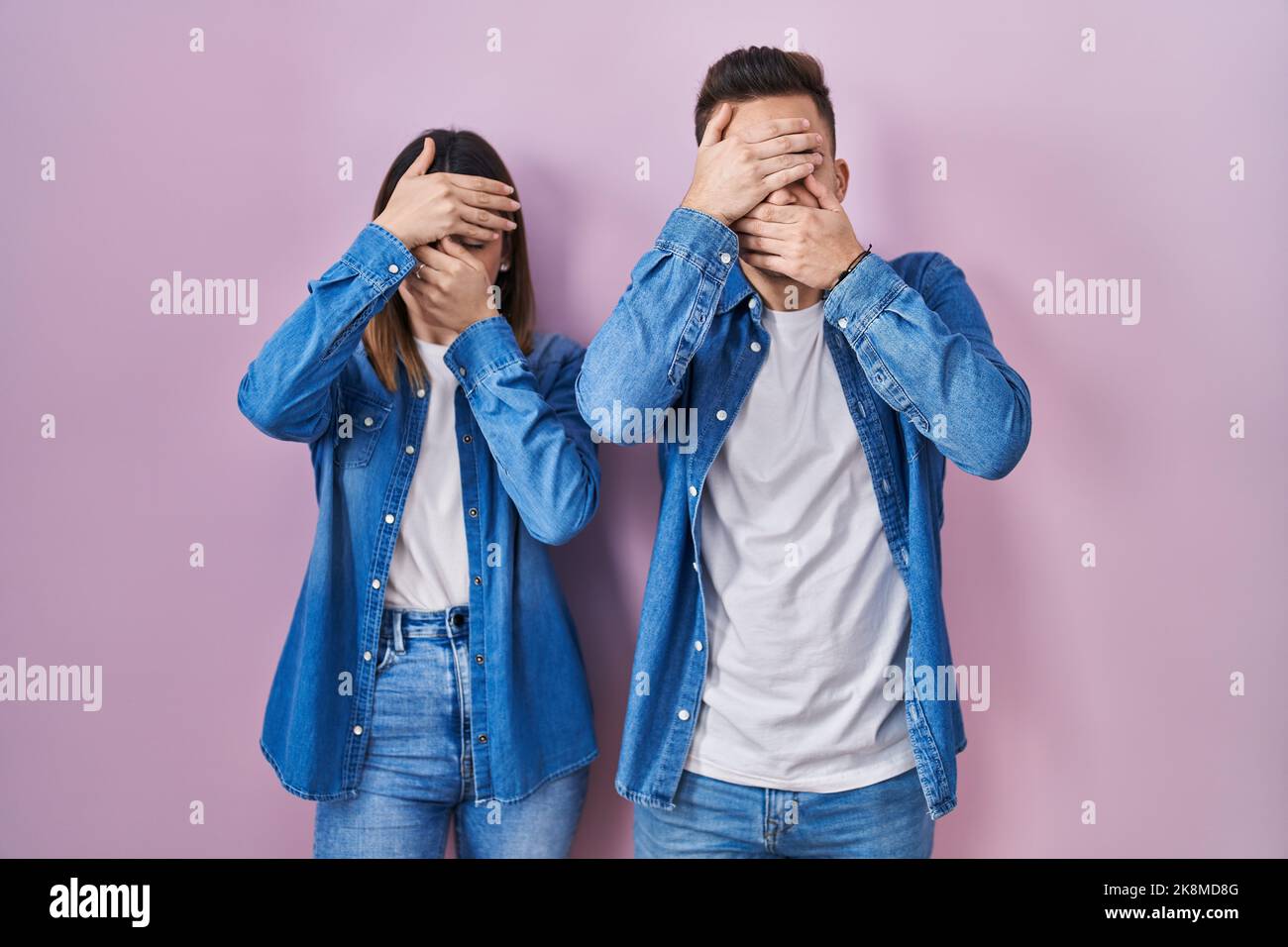 Young hispanic couple standing over pink background covering eyes and ...