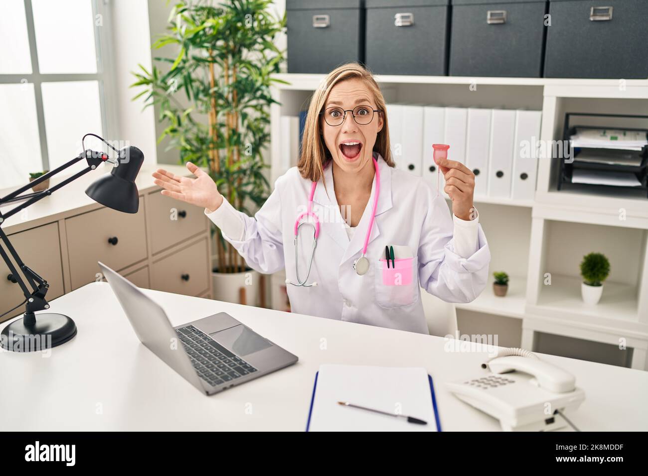 Young blonde doctor woman holding menstrual cup celebrating achievement ...