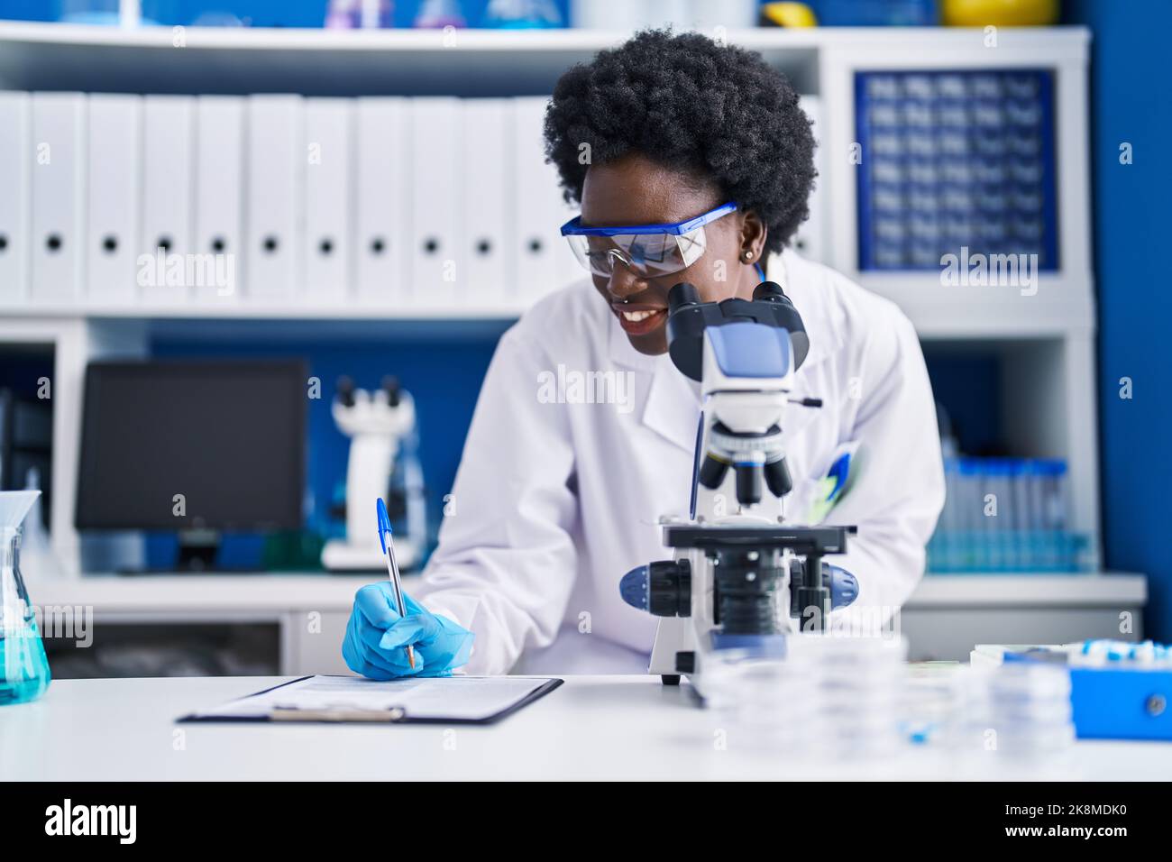 Young african american woman scientist writing on document using microscope at laboratory Stock ...