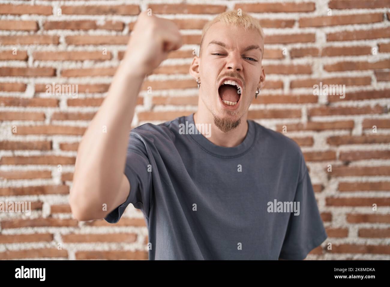 Young caucasian man standing over bricks wall angry and mad raising ...