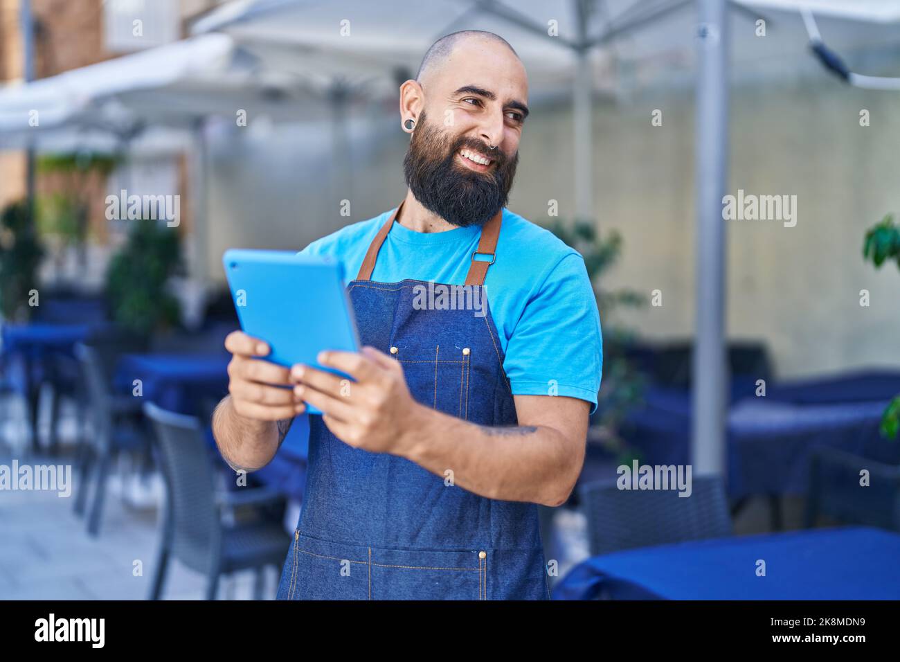 Young bald man waiter smiling confident using touchpad at coffee shop ...
