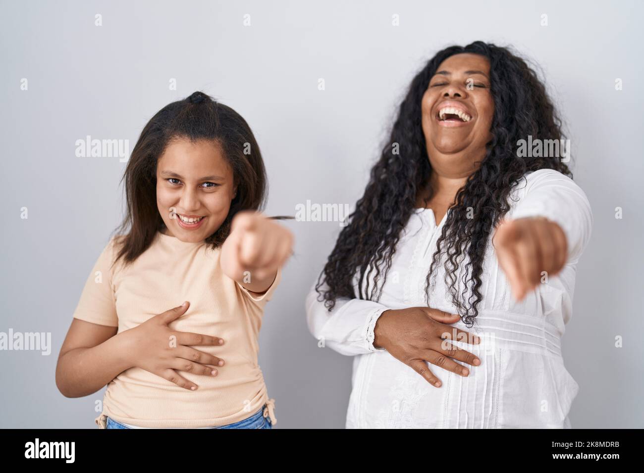 Mother and young daughter standing over white background laughing at ...