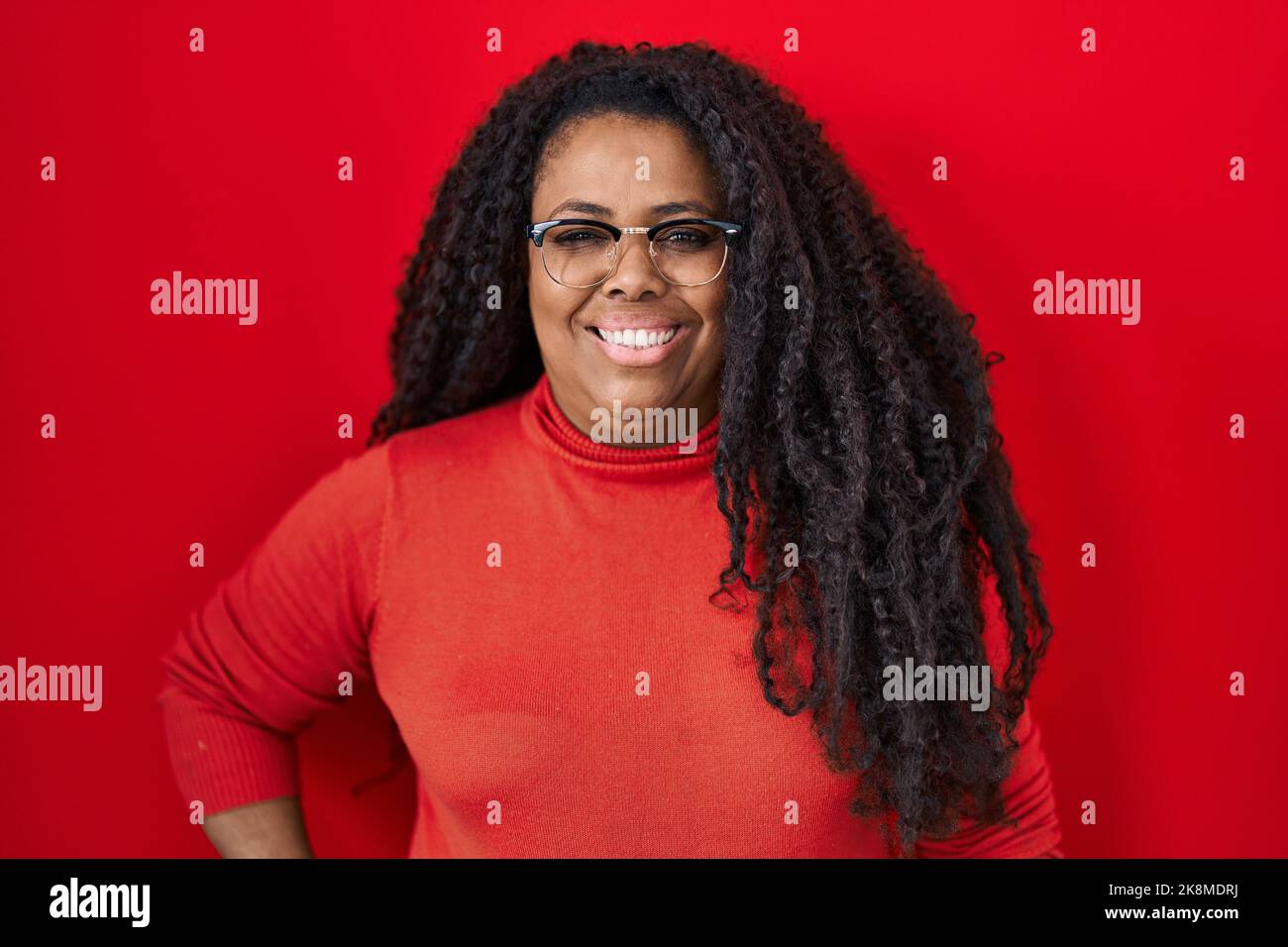 Plus size hispanic woman standing over red background with a happy and ...