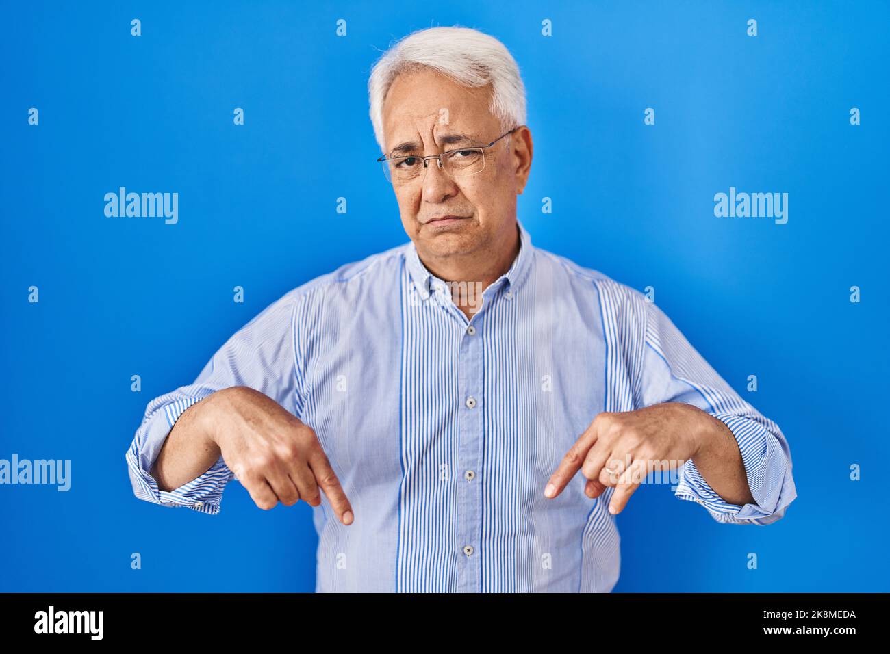 Hispanic senior man wearing glasses pointing down looking sad and upset ...