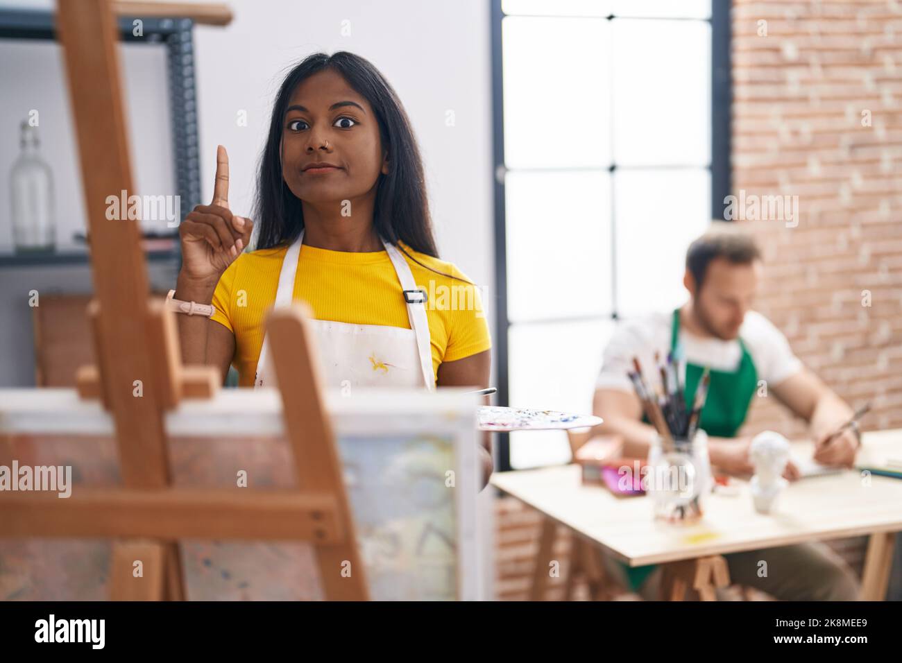 Indian woman at art studio smiling with an idea or question pointing ...