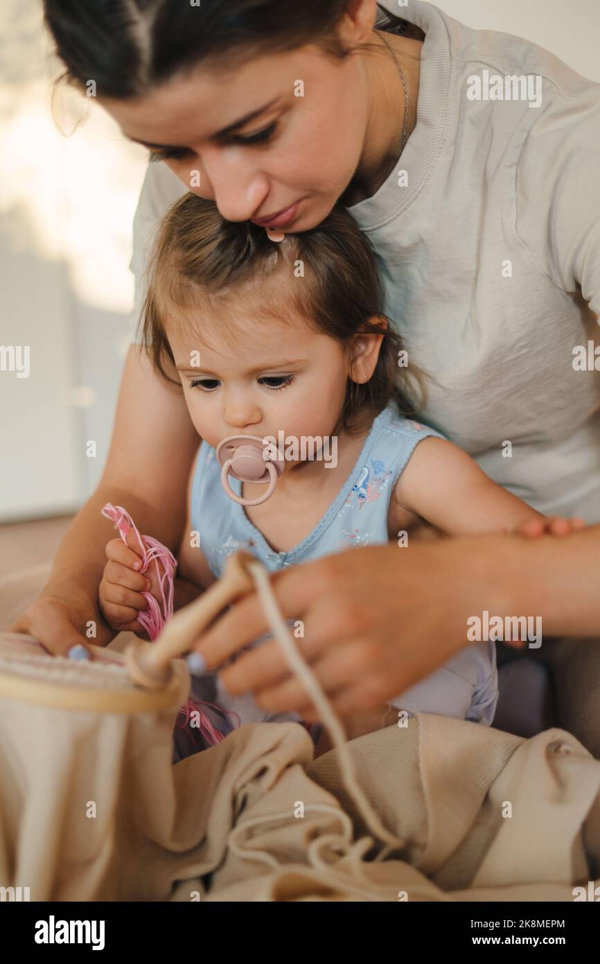 Female teaching baby girl how to embroider a pattern on the white ...