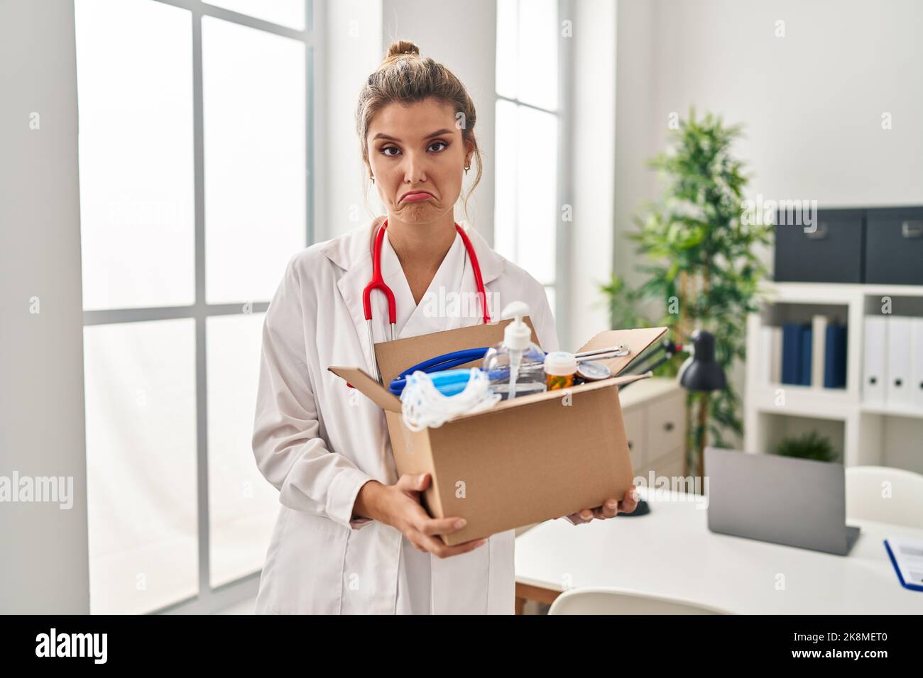 Young doctor woman holding box with medical items depressed and worry ...