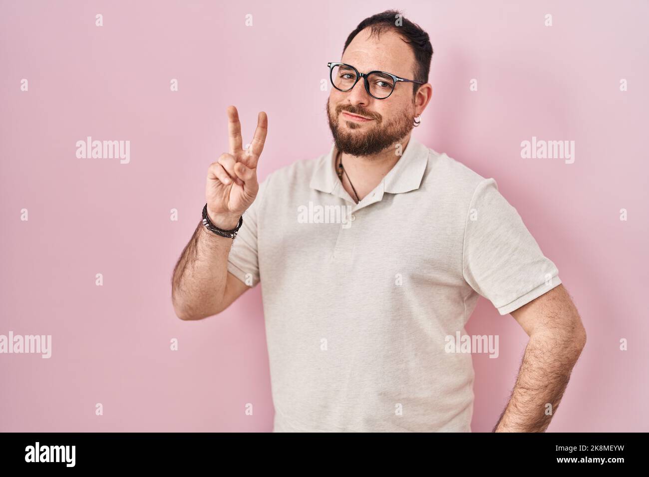 Plus size hispanic man with beard standing over pink background smiling ...