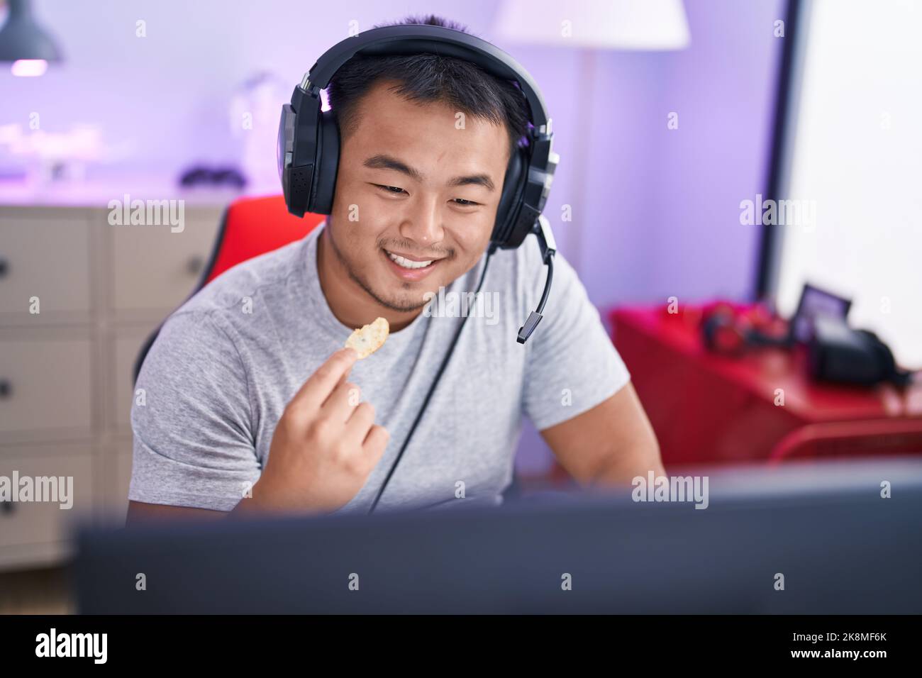 Young chinese man streamer playing video game eating chips potatoes at ...