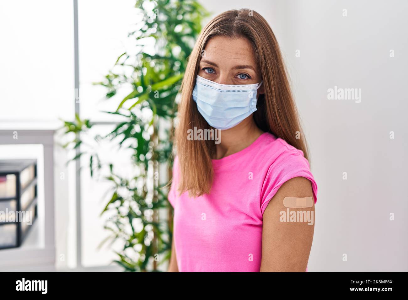 Young woman getting vaccine showing arm with band aid thinking attitude ...