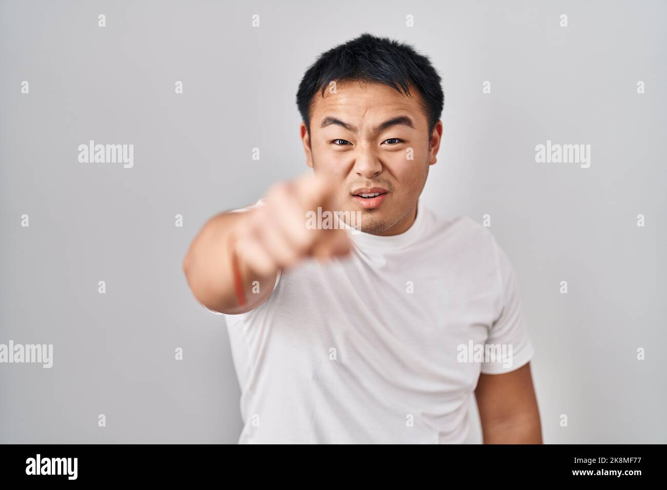 Young chinese man standing over white background pointing displeased ...