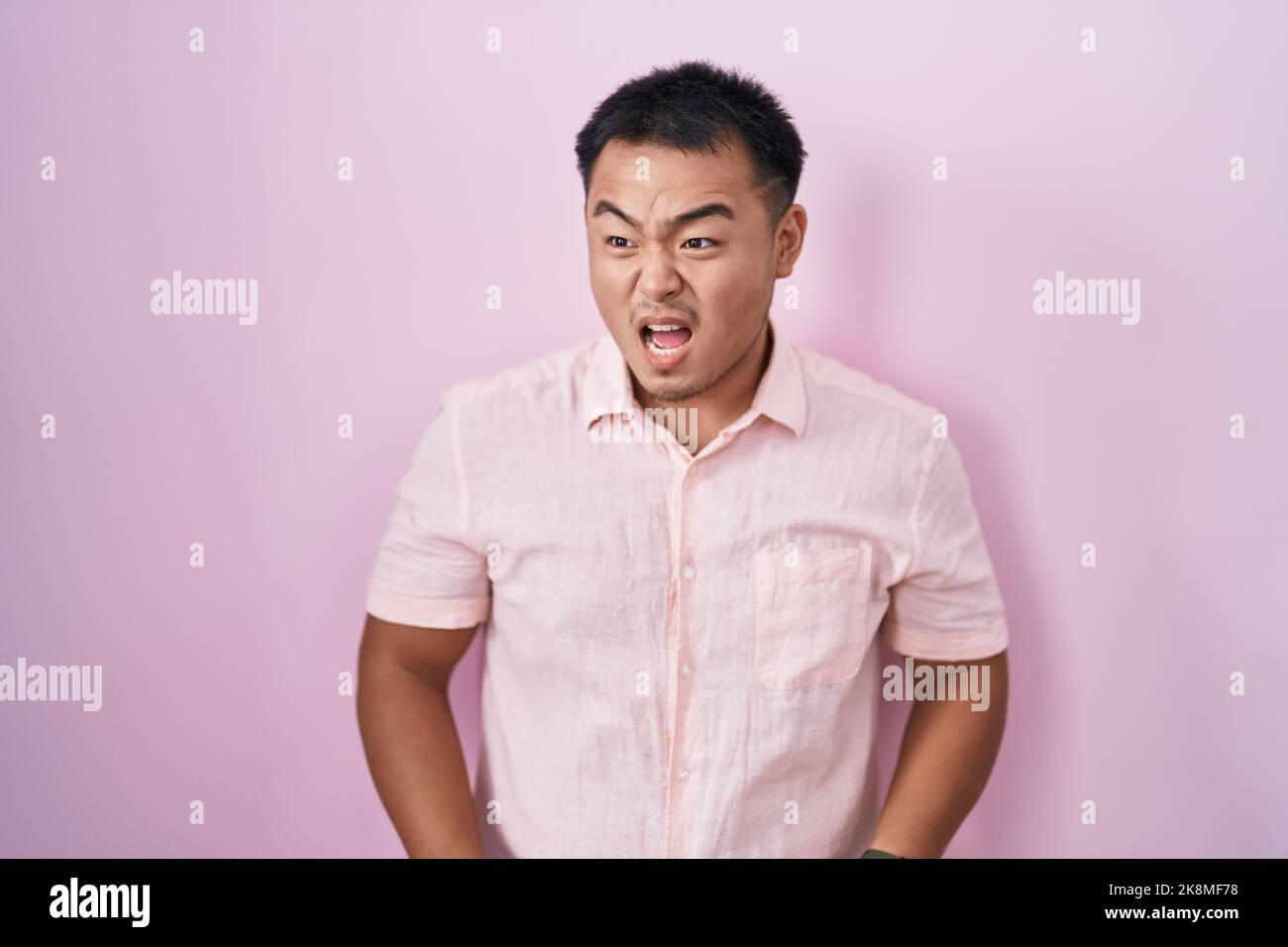 Chinese young man standing over pink background angry and mad screaming ...