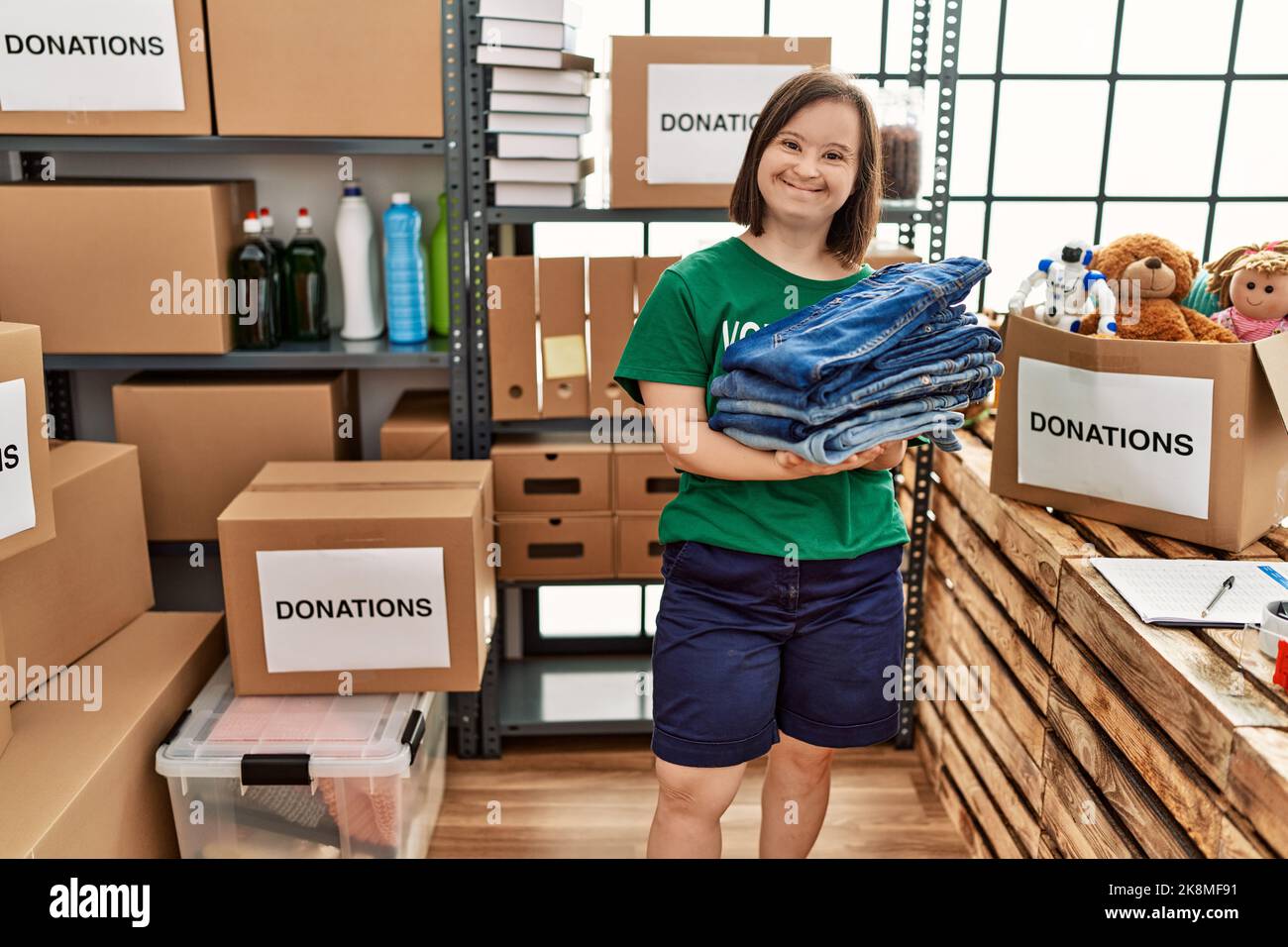 Brunette woman with down syndrome holding folded jeans at donations ...