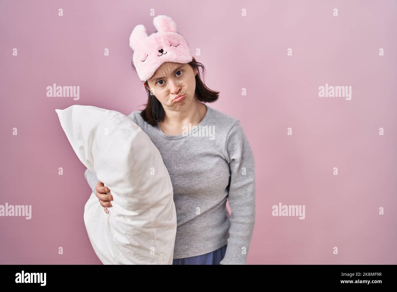 Woman with down syndrome wearing sleeping mask hugging pillow depressed ...