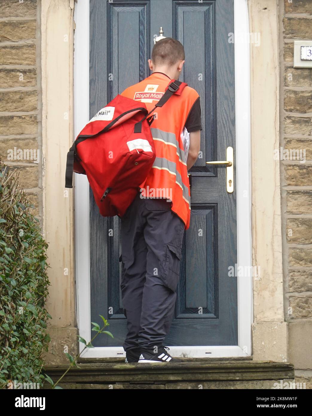 A postman delivers mail to a house in New Mills, Derbyshire Stock Photo ...