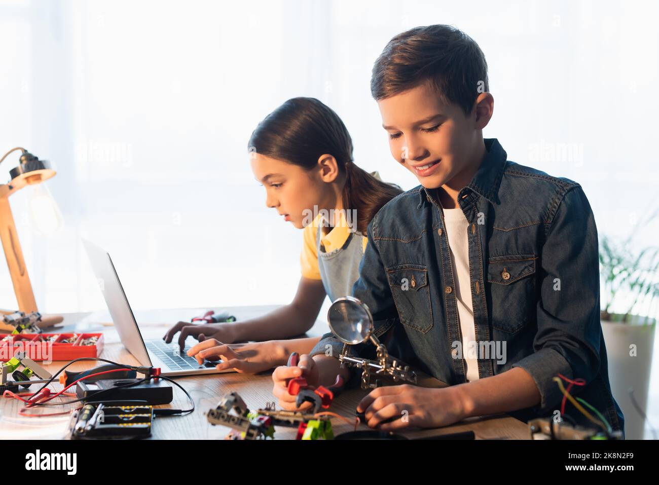 smiling boy with magnifier assembling robotics model near girl using laptop,stock image Stock ...