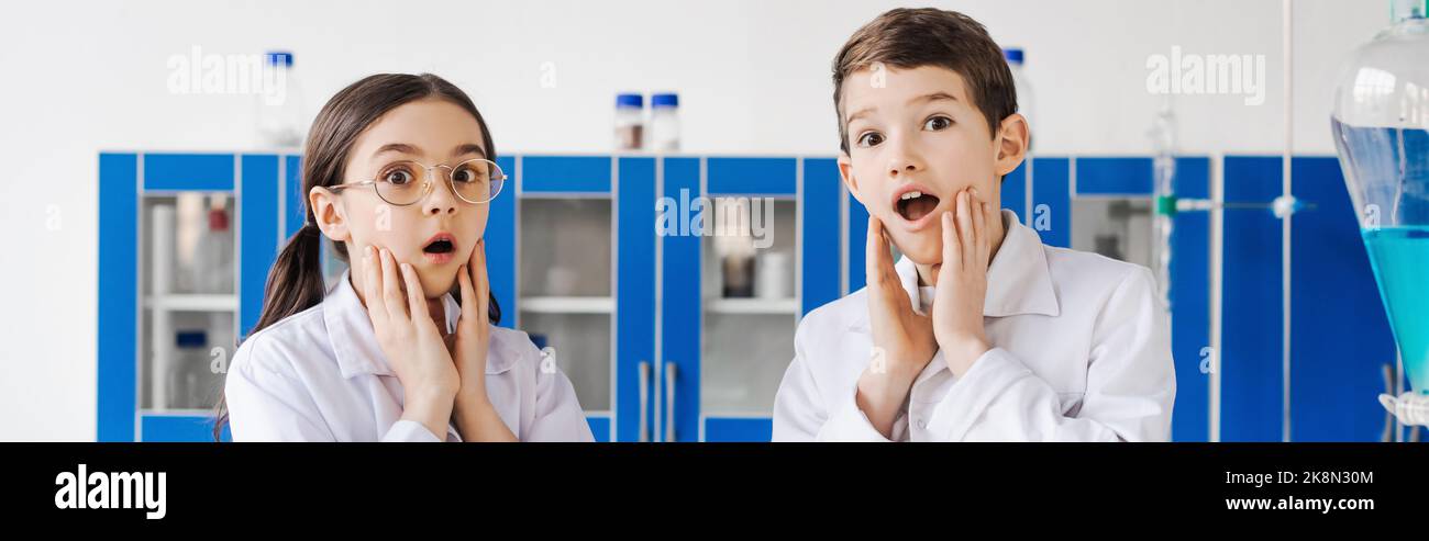 shocked kids in white coats touching faces and looking at camera in ...