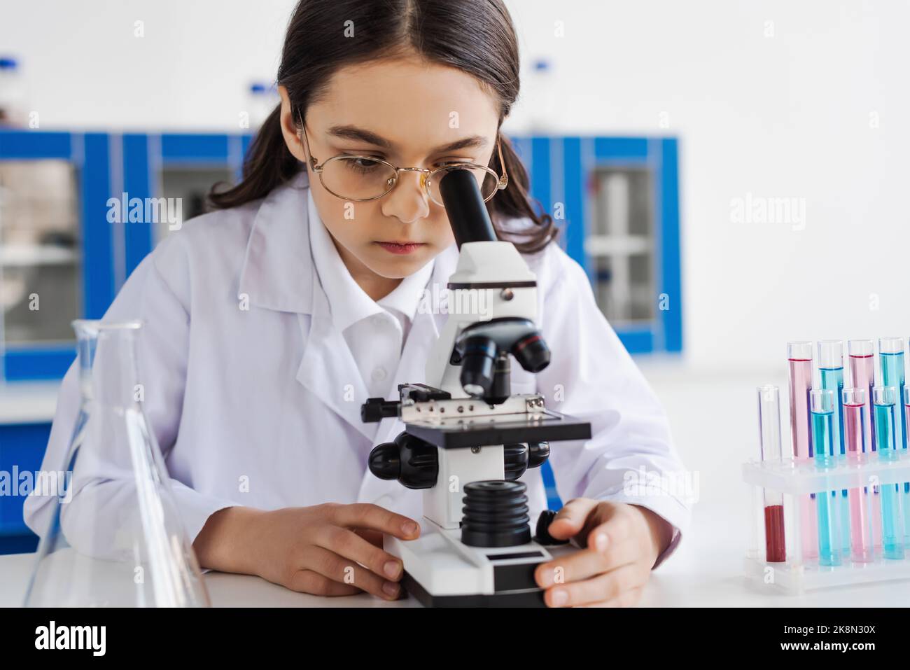 brunette girl in white coat and eyeglasses using microscope in lab ...
