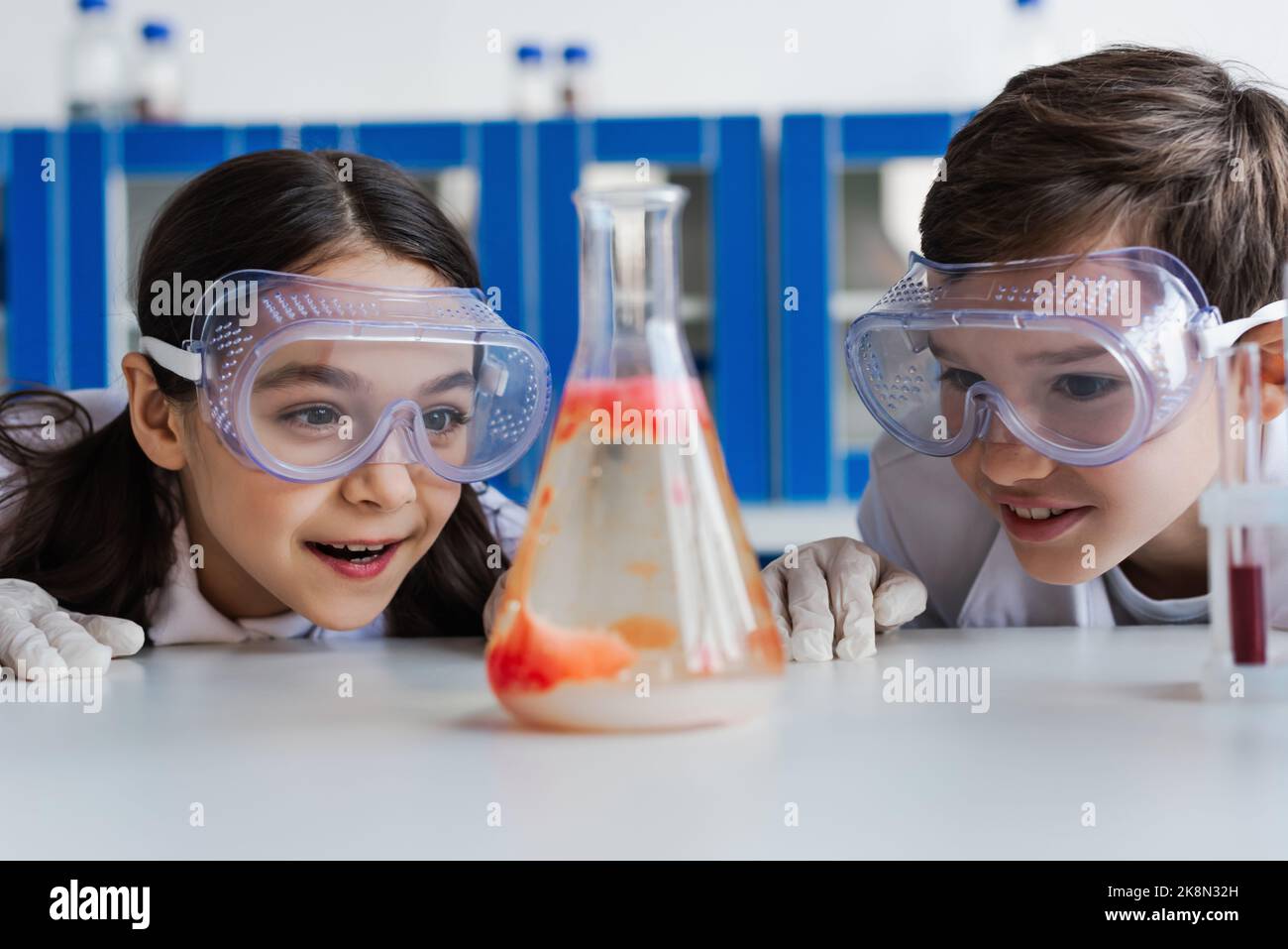 amazed kids in goggles looking at blurred flask with liquid while doing ...