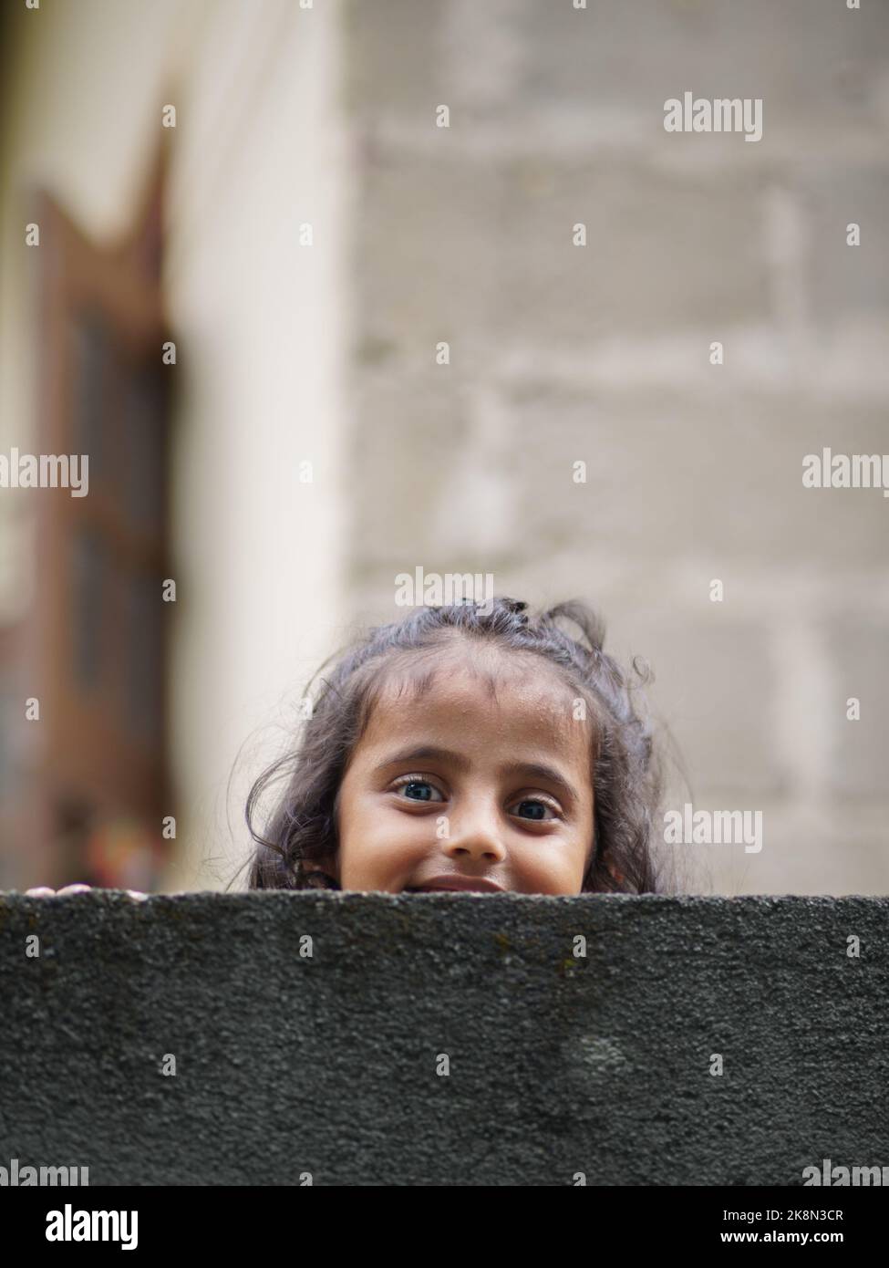 An adorable little girl peeking behind a high concrete wall Stock Photo ...