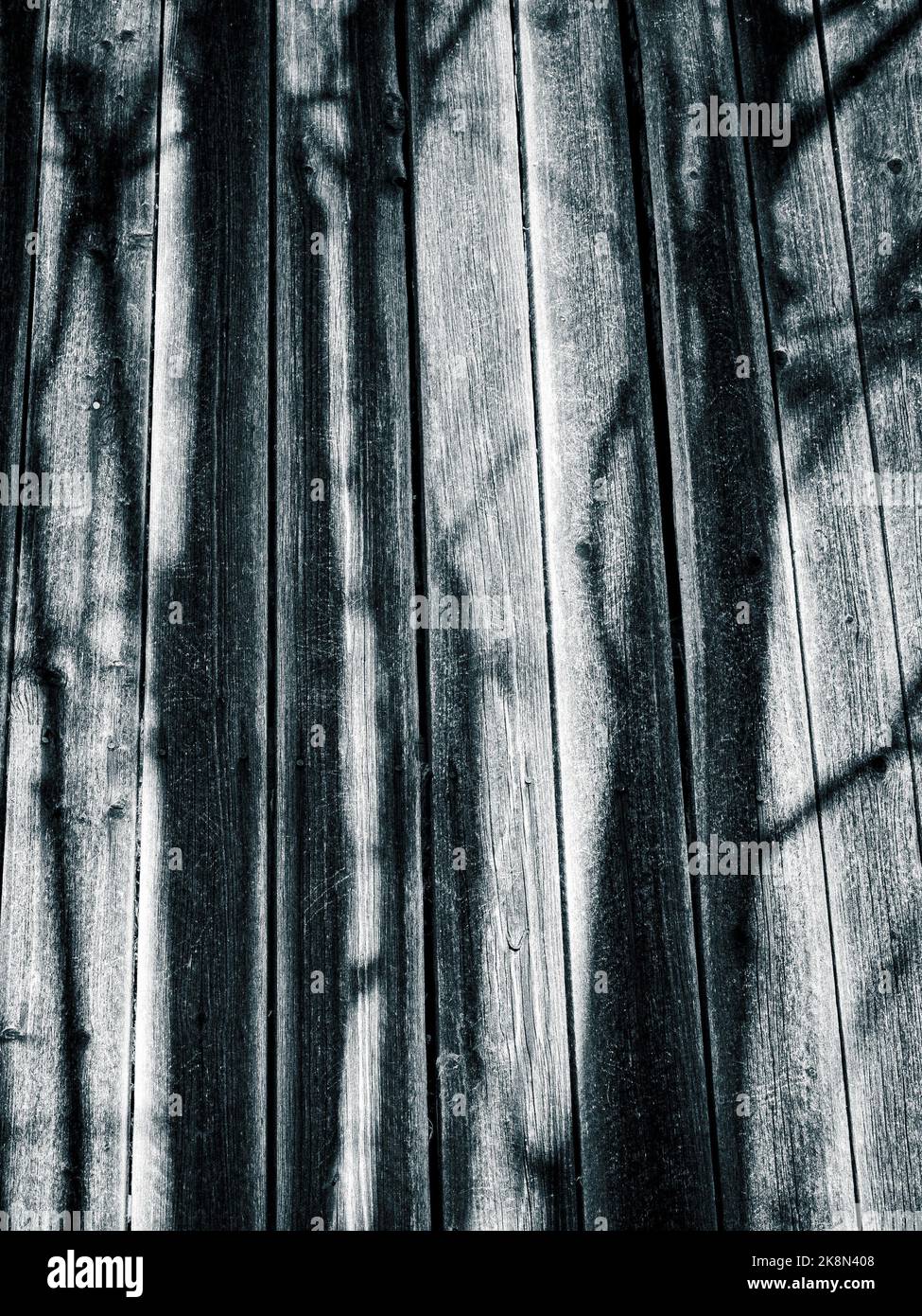 A vertical shot of shadows of trees on an the wooden wall of an old ...