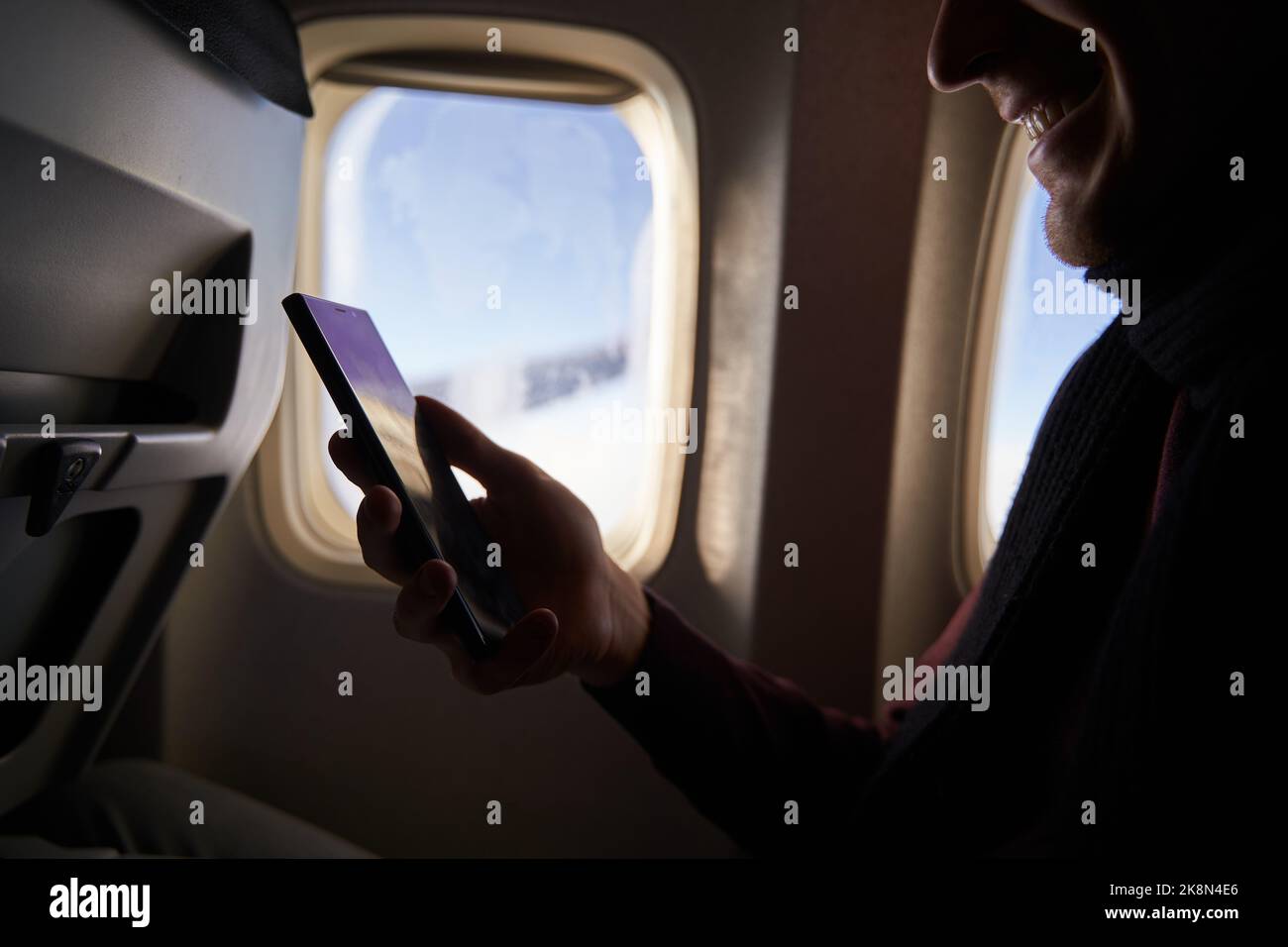 Businessman sitting next to airplane window and using smartphone ...
