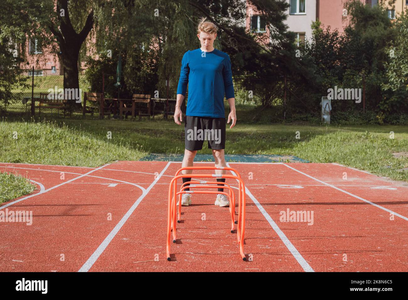 Blond boy in sportswear jumps over red obstacles to improve lower body ...