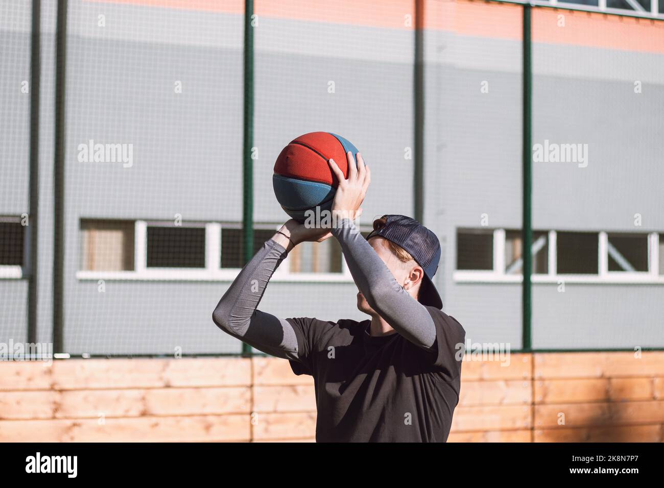 Blond boy in sportswear practices shooting a basketball from behind the ...