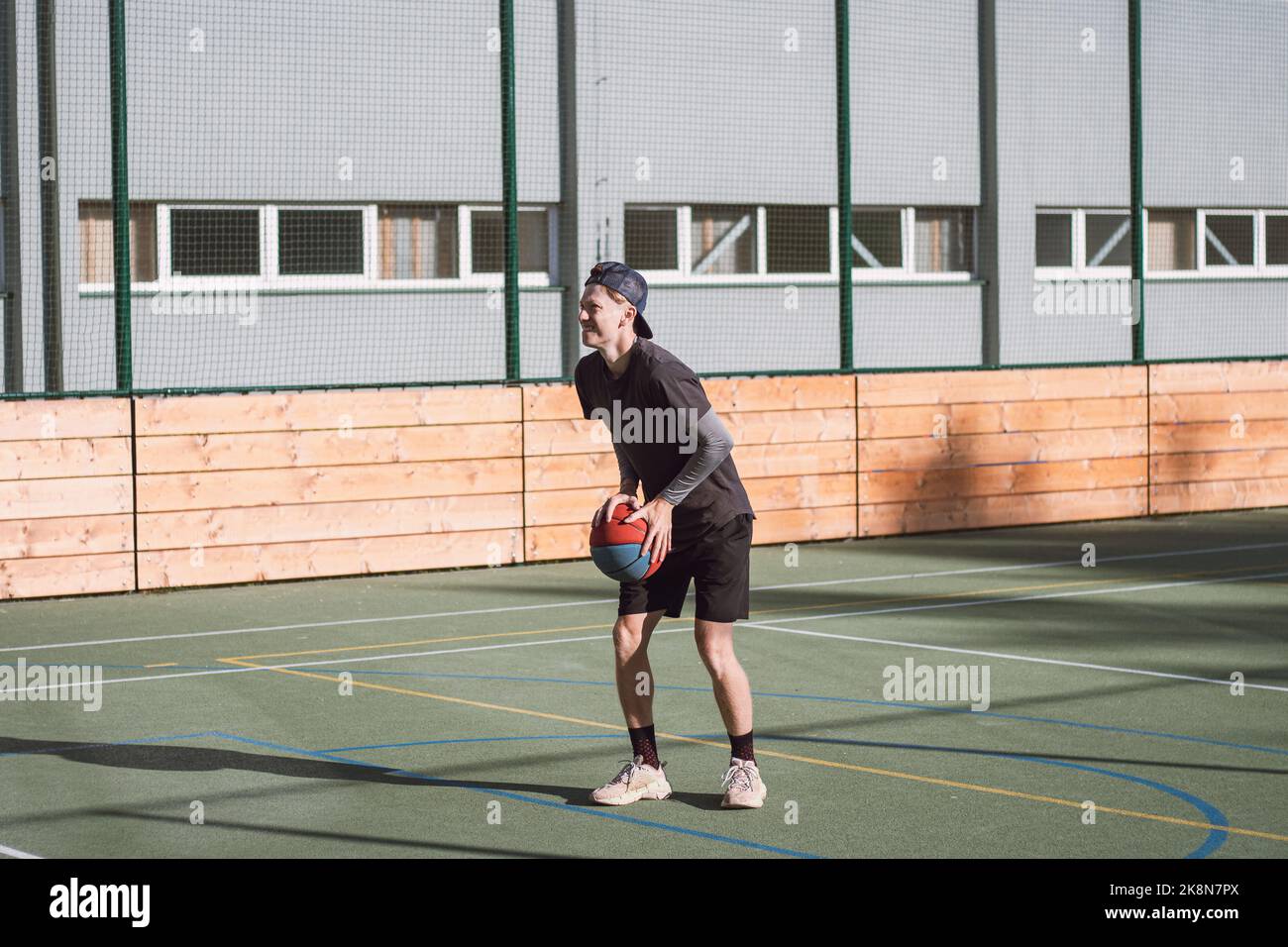Blond boy in sportswear practices shooting a basketball from behind the ...