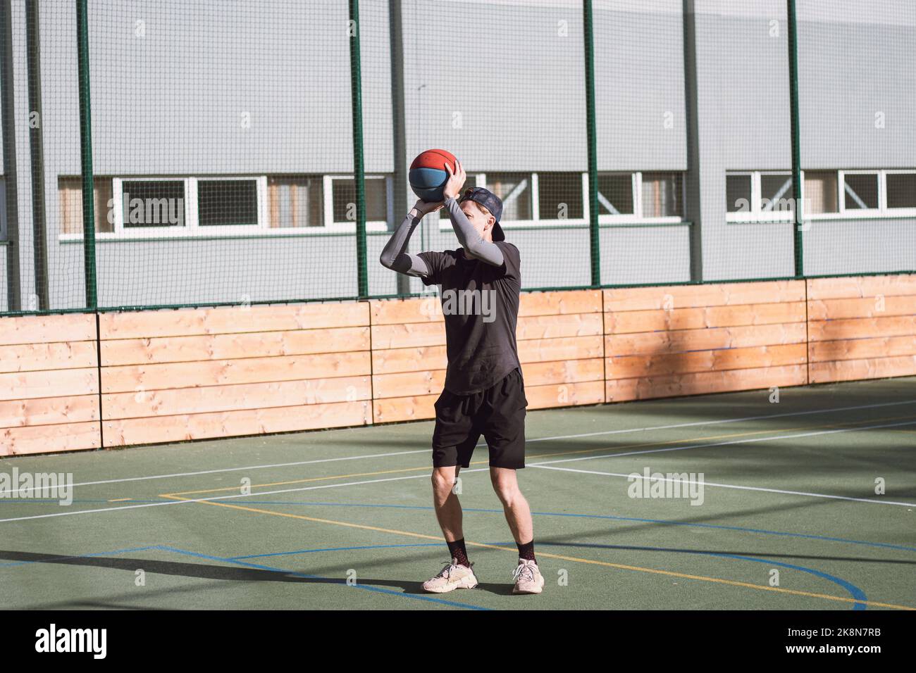 Blond boy in sportswear practices shooting a basketball from behind the ...