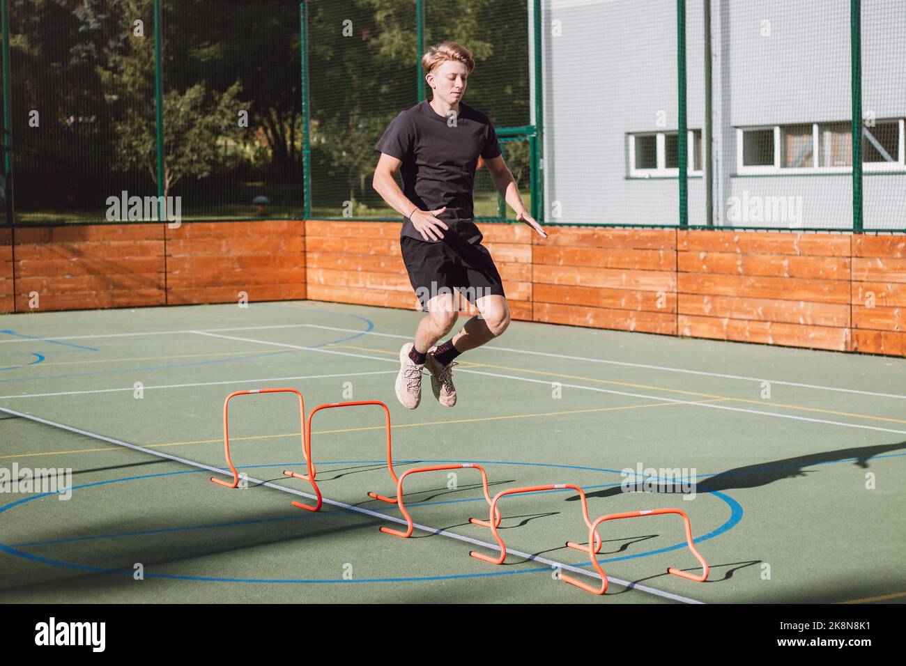 Blond boy in sportswear jumps over red obstacles to improve lower body ...