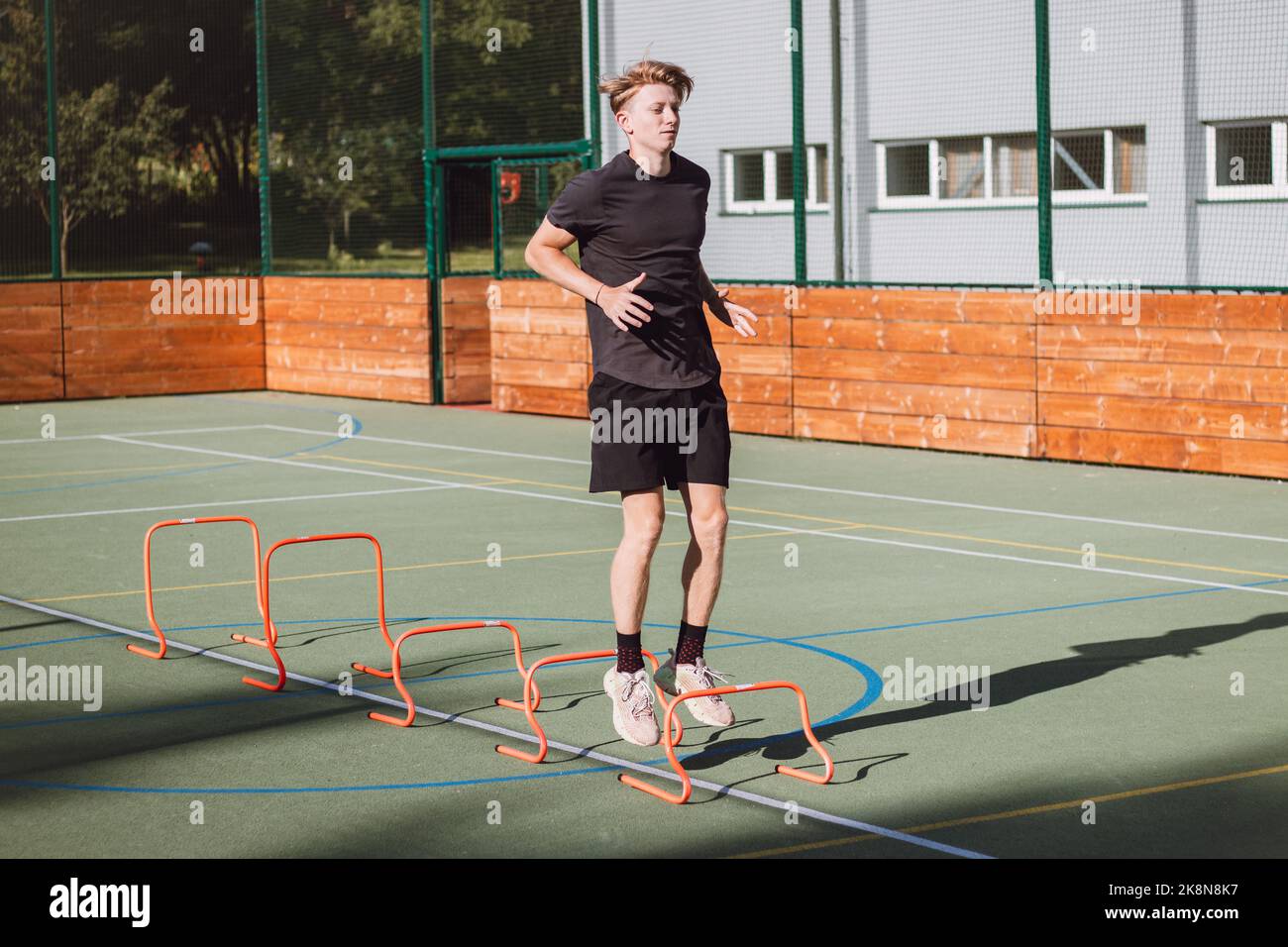 Blond boy in sportswear jumps over red hurdles to improve lower body ...