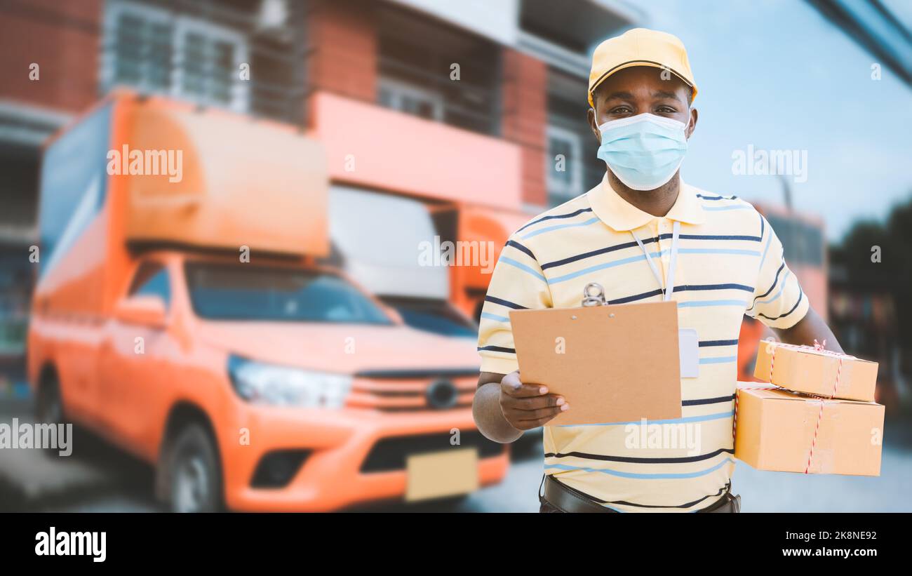 African delivery man in face mask holding a box package and cardboard ...
