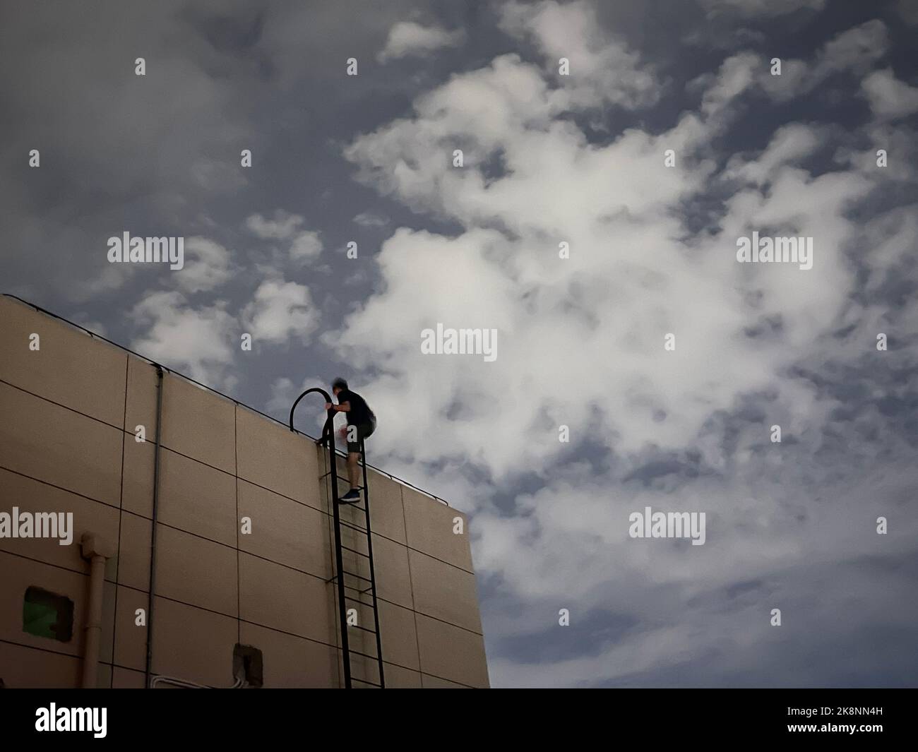 A man climbing a metal ladder on a rooftop of a high residential ...