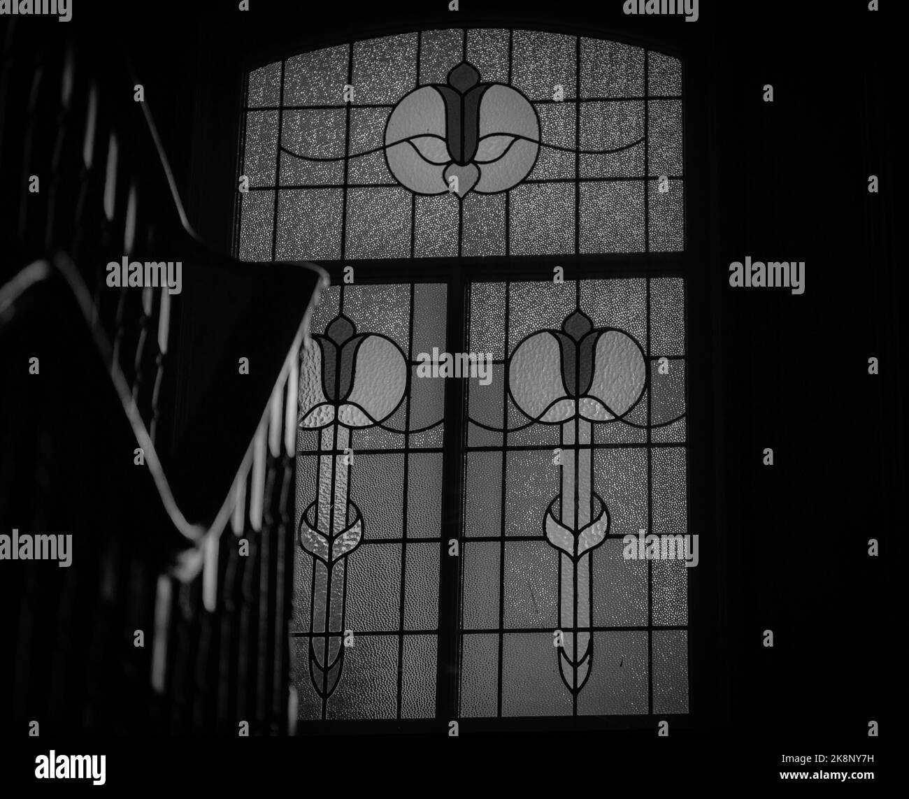 A grayscale shot of a stained glass window at night with stairs railing ...