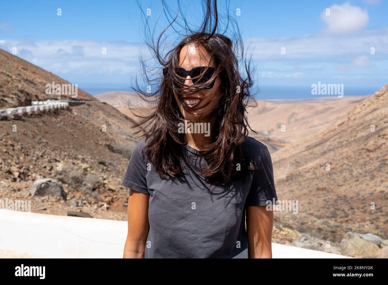 Portrait of young smiling woman face partially covered with flying hair ...