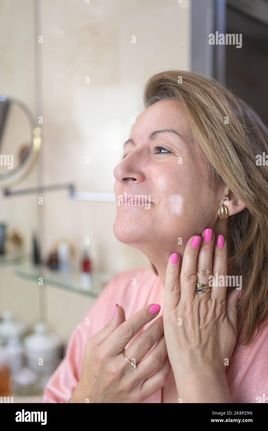 Adult white woman applying cosmetics and cream on the face and neck for ...